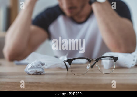 depressed student studying at table with crumpled papers and eyeglasses ...
