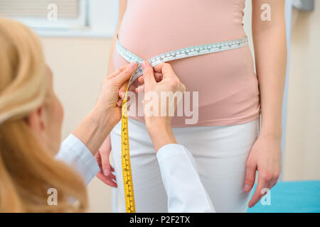 cropped shot of obstetrician gynecologist measuring belly size of ...