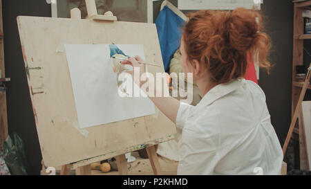 Female artist painting still life subjects in studio surrounded by ...