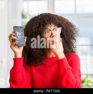Young woman holding broken smartphone showing cracked screen looking ...