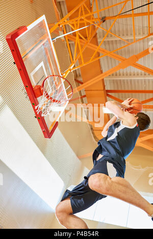 From below young sportsman throwing ball into basket while training ...