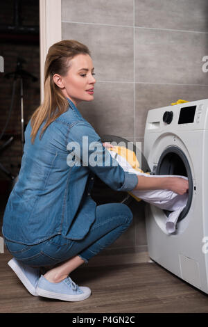 Beautiful woman taking laundry out of washing machine on white ...