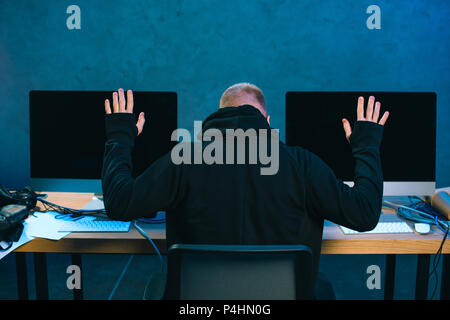 Rear view of hacker in front of computer with multiple screens in dark ...