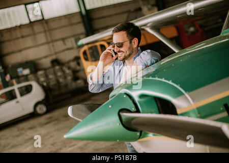 Young handsome young pilot checking airplane in the hangar and using ...