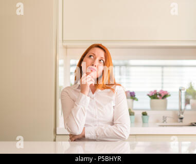 Redhead woman at kitchen with serious expression on face. Simple and ...