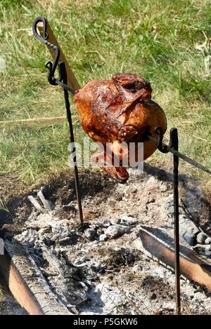 Slow cooking chicken over a campfire in the outdoors during the middle ...