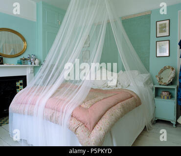 White voile drapes above bed with white linen in cottage bedroom with ...