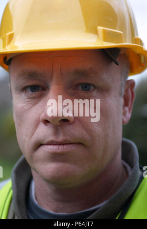 A construction worker wearing a hard hat and safety harness is securing ...
