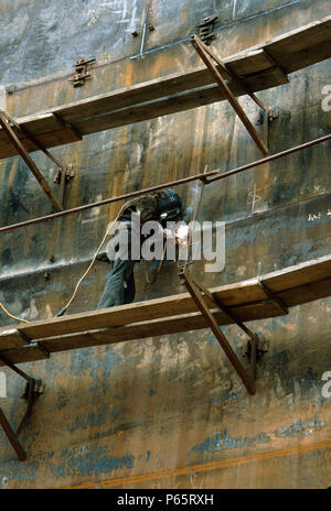 A man welding steel plates on the hull of a new tugboat under ...