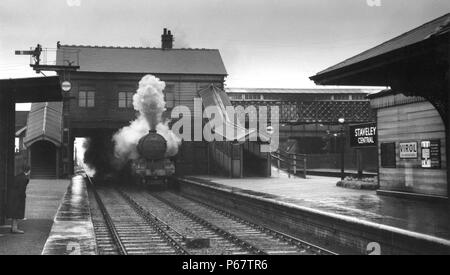 Gresley V2 Class emerging from beneath the footbridge on a wet and grey ...