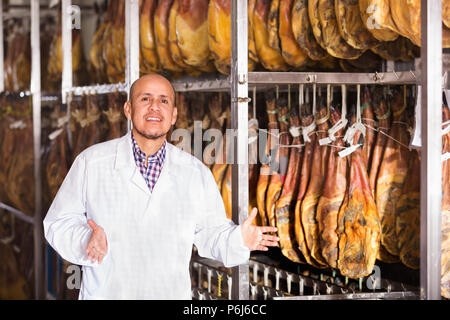 Middle age cheerful technologist with joints of serrano jamon at farm ...