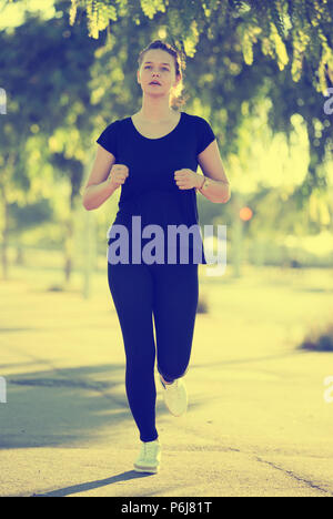 Sporty svelte girl jogging during outdoor daily workout with music ...