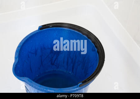 Collecting cold water in blue bucket from shower waiting for warm water ...