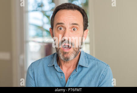 Handsome senior man at home afraid and shocked with surprise expression ...