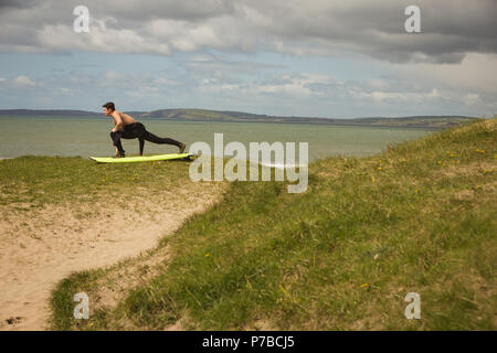 Surfer with surfboard performing stretching exercise at beach Stock ...