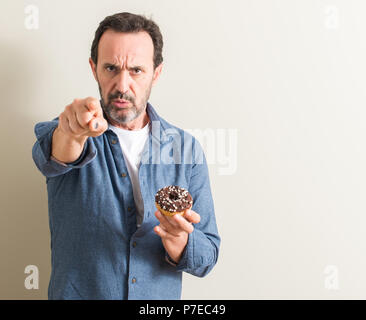 Senior man eating chocolate donut with a happy face standing and ...