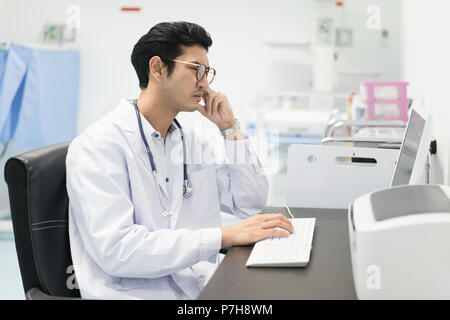 Asian medical professional sitting at desk using laptop while talking ...