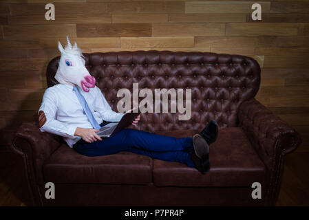 Funny unicorn in suit sits on sofa like a boss. Unusual man resting at ...