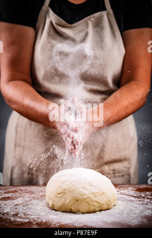 Woman sprinkling flour on dough against dark background Stock Photo - Alamy