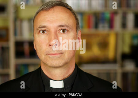 A good looking serious catholic priest is studying, reading the Bible ...