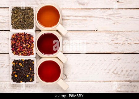 Various kind of tea in mugs and small square plates with dry tea on ...