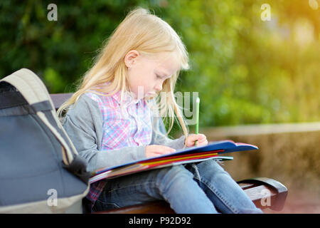 Adorable little schoolgirl studying outdoors on bright autumn day ...