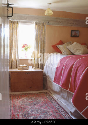 Wooden chest below window in cottage bedroom with cushions and red ...