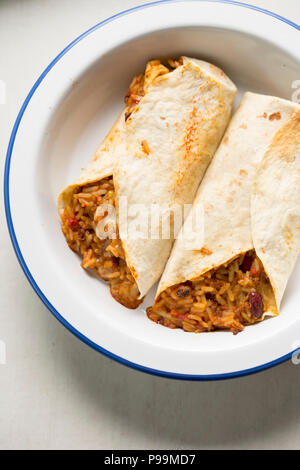Beef burrito with rice and beans wrapped in silver paper on stone plate ...