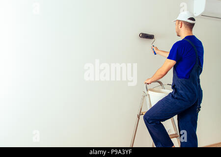 Rear view of painter man looking at white wall, with paint roller and ...