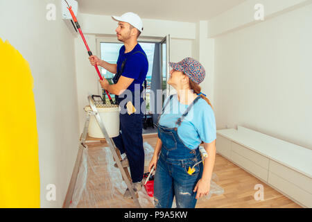 Man decorator coloring wall with yellow color while standing on ladder ...