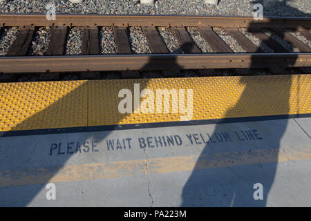Warning sign on station platform edge with non slip paving and yellow ...