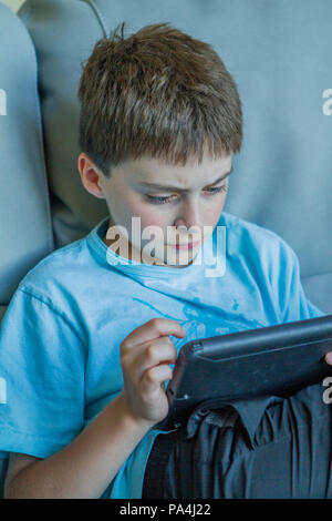 Teen age boy and his iPad, concentrating. A youbger blonde girl is ...