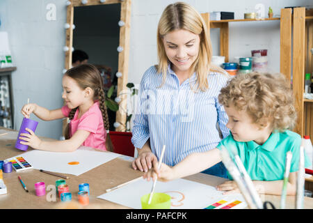 Mother teaching children in drawing class. Daughter and son painting ...