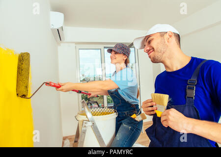 Couple wearing blue overalls painting their living room in yellow color ...