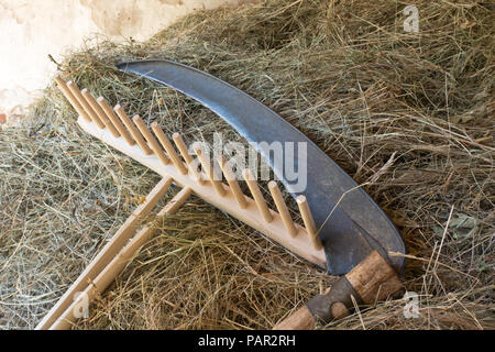 A scythe and a rake with hay Stock Photo - Alamy