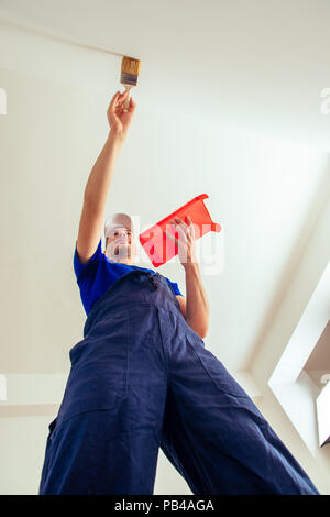 Painter in overall with paintbrush coloring wall in white Stock Photo ...