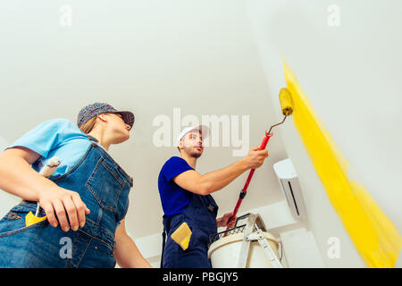 Couple wearing blue overalls painting their living room in yellow color ...