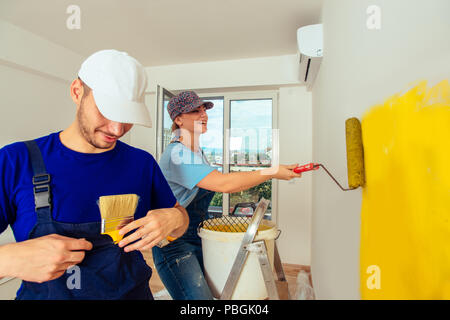Couple wearing blue overalls painting their living room in yellow color ...