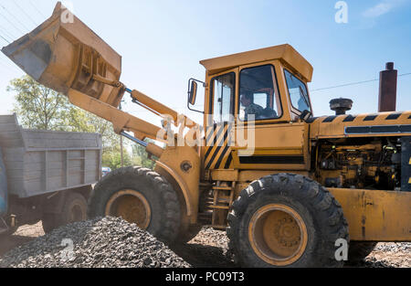 Yellow loader delivering stone gravel into truck during road ...