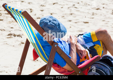 Man snoozing on chair with hat over eyes Stock Photo - Alamy