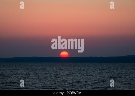 Big red sun rising over lake scene Stock Photo - Alamy