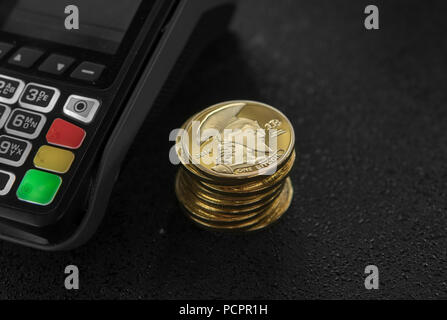 A pile of gold Titan coins and POS terminal with a hindred dollar ...