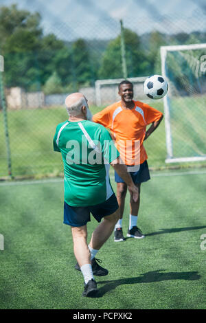 multiracial old men playing football together on green field Stock ...