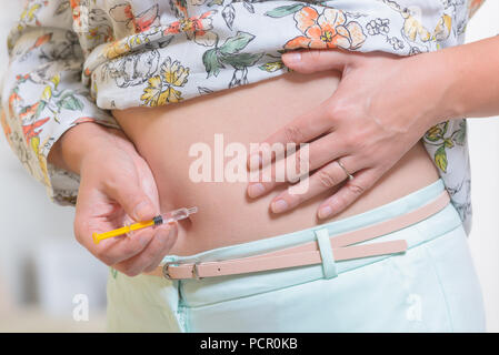 Woman is doing an insulin or heparin injection in her abdomen at home ...