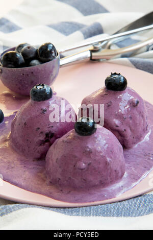 Blueberry ice cream balls with icecream scoop on a pink plate over ...