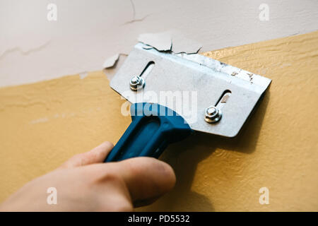 Close-up. A man with a scraper removes the old covering from the wall ...