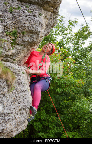 Photo of athlete girl clambering over rock against background of green ...
