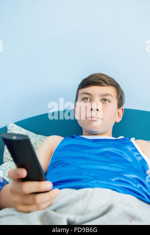 Caucasian teenage boy flicking through tv channels with a remote ...