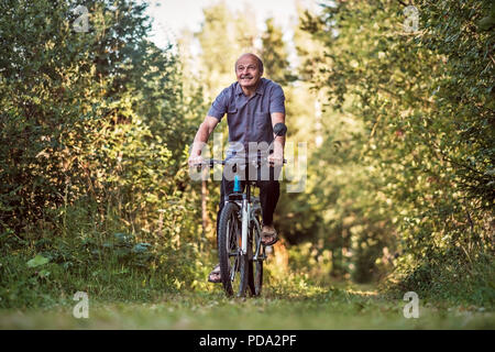 Joyful senior man riding a bike in a park on a beautiful sunny day ...