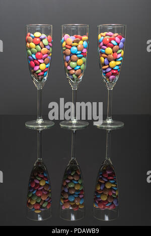 Three champage flute glasses filled with smarties and isolated on black ...